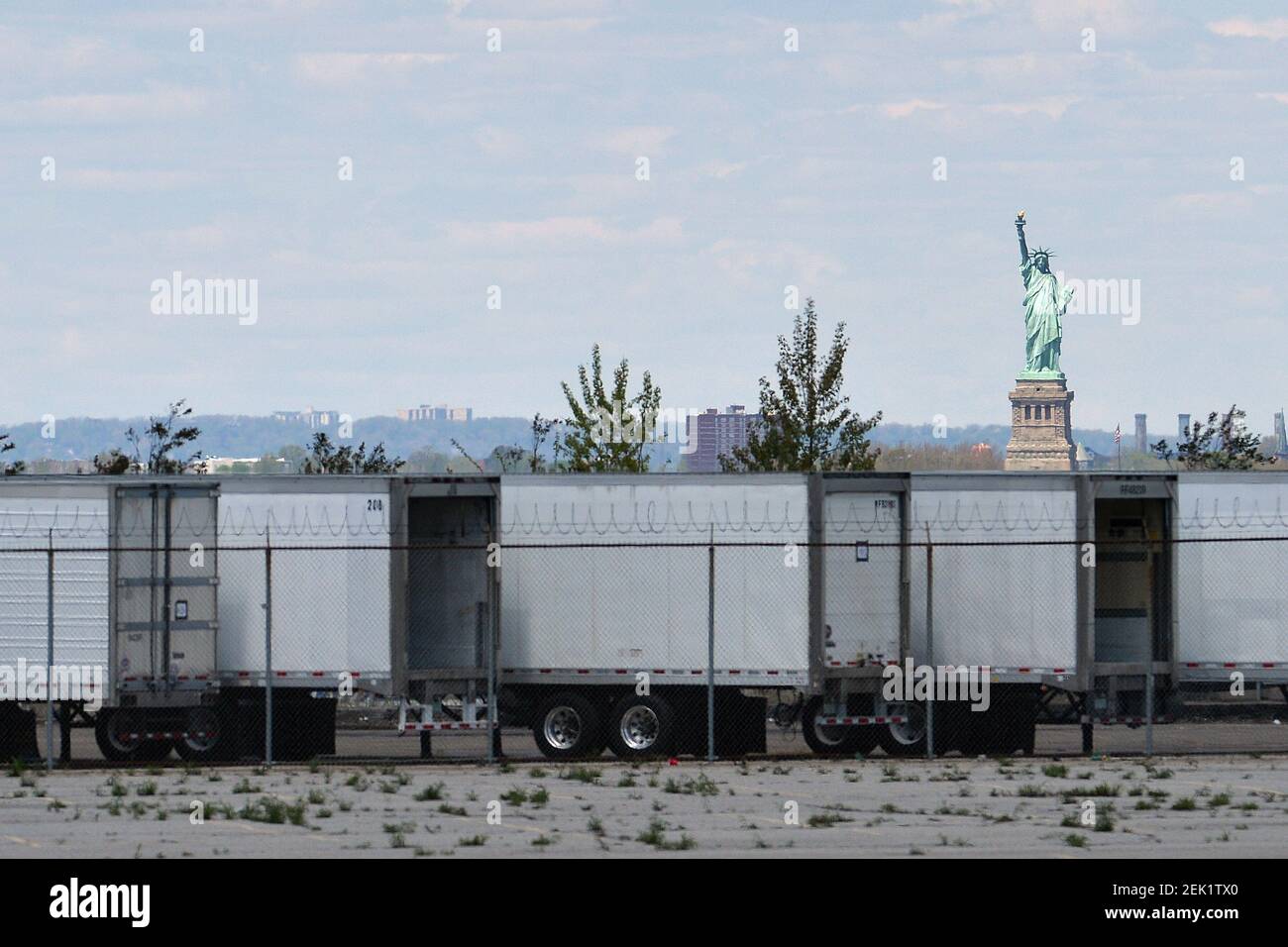 The Statue of Liberty can be seen behind a row of refrigerator trucks ...