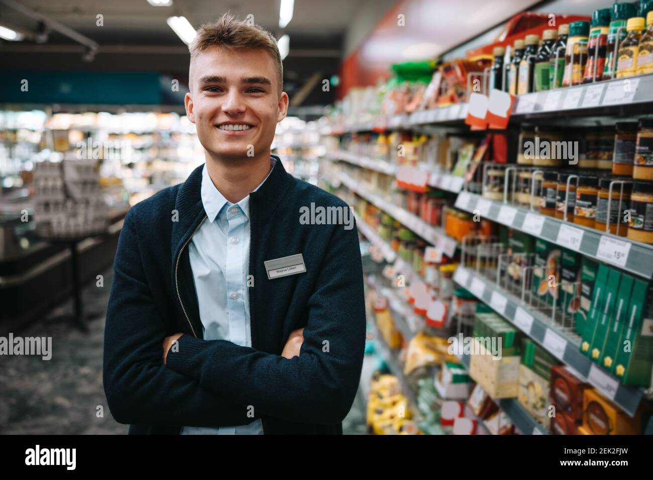 Portrait of a man in uniform standing at with arms crossed at grocery ...