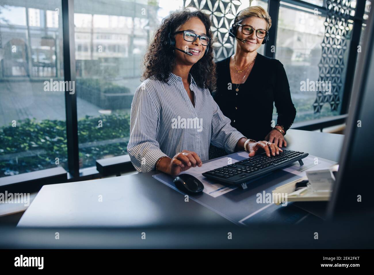 Smiling call center workers at the office desk. Two female coworkers ...