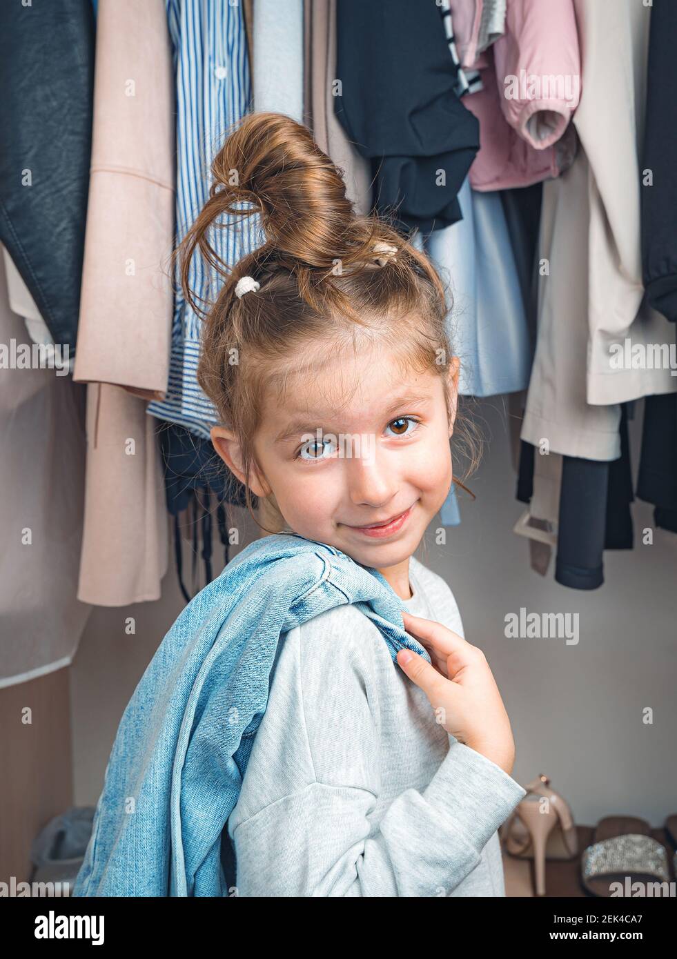 Cute little girl smiles against the background of clothes on hangers in ...