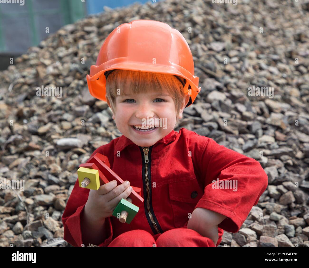 cute boy in orange construction helmet and red work overalls sits on ...