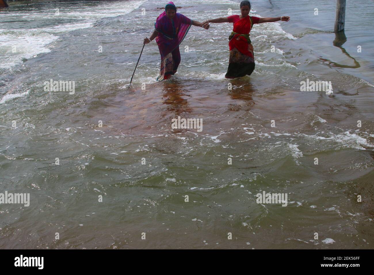 Women are seen crossing a flooded road on the flooded embankment of the ...