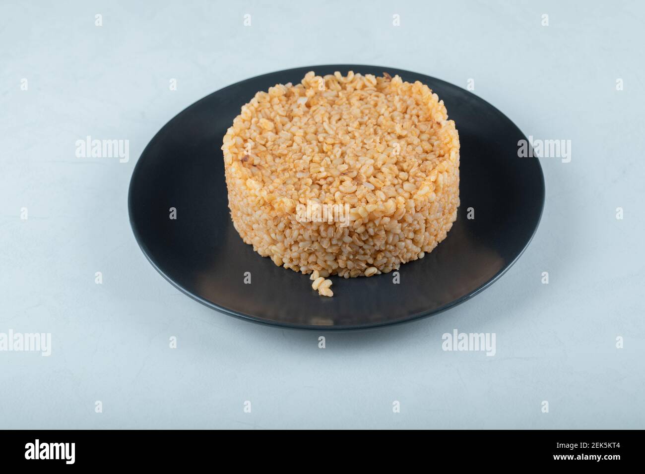 Bulgur rice on dark plate on a white background Stock Photo - Alamy