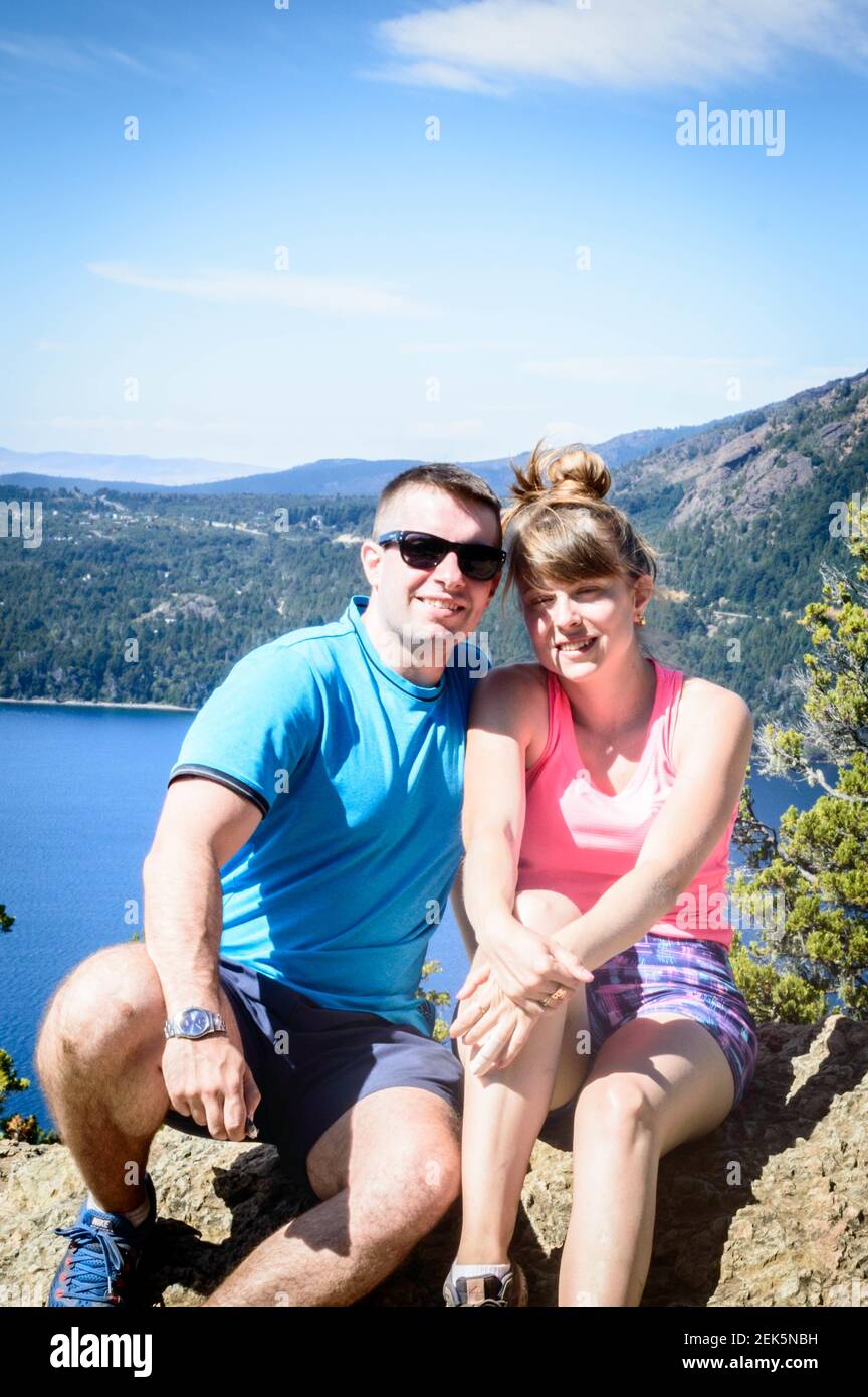 Cute young couple sitting on top of a cliff and taking a photo with a ...