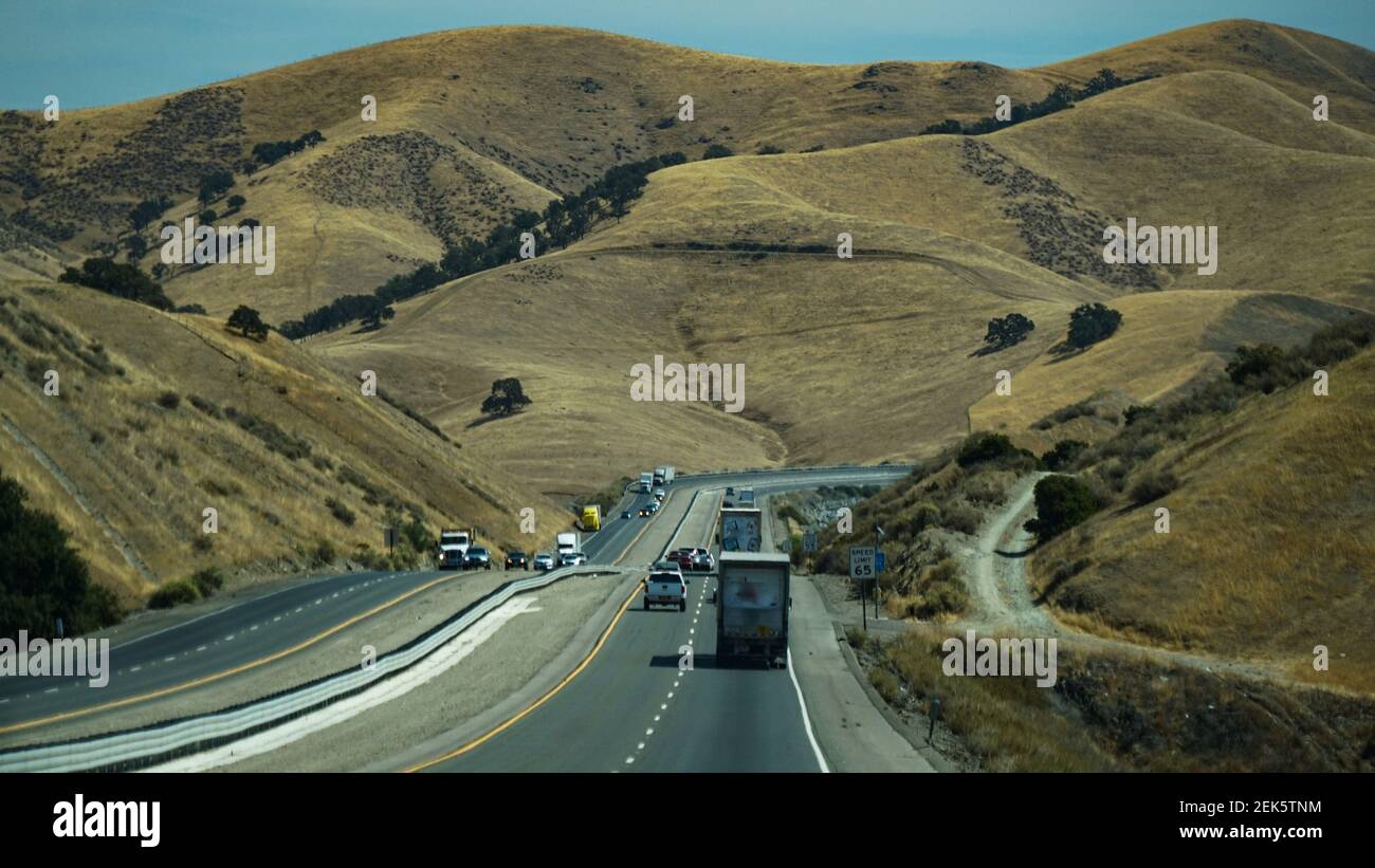 Vehicles driving through the afternoon sun in a hilly landscape in ...