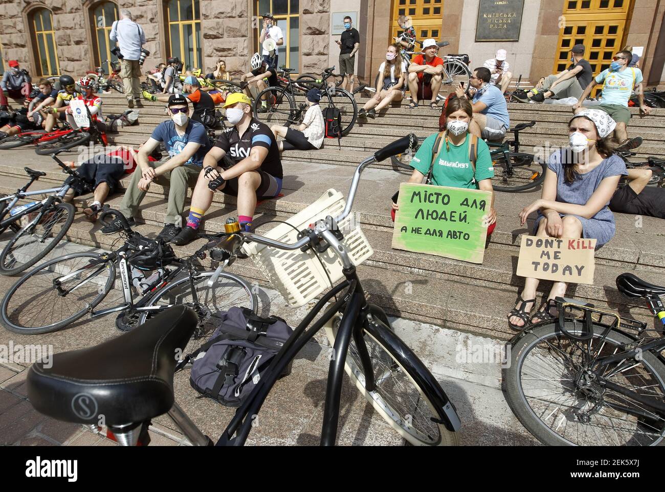 Cyclists sit on stairs while holding placards during the protest ...