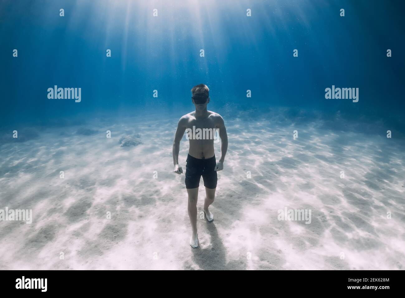 Sporty man freediver stay on sandy bottom underwater in tropical sea ...