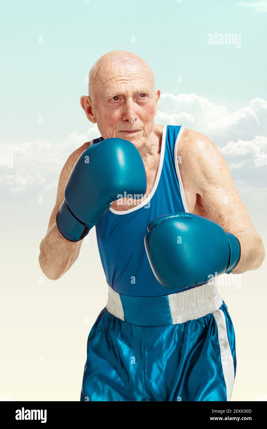 Senior man wearing sportwear boxing isolated on sky background ...