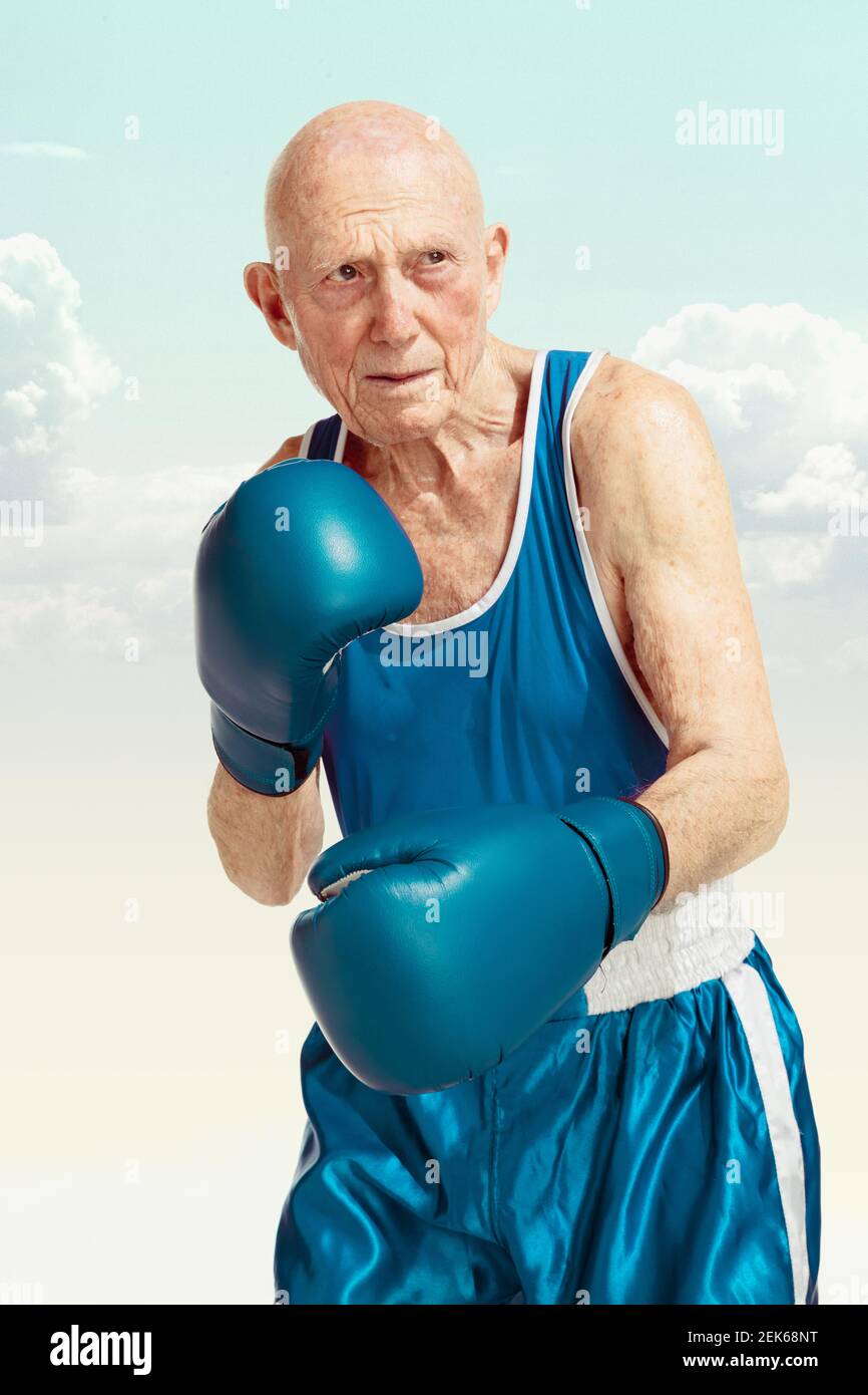 Senior man wearing sportwear boxing isolated on sky background ...