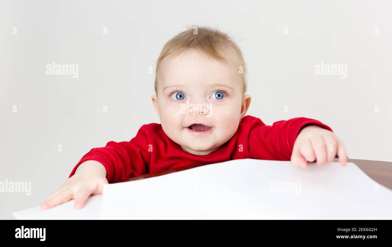 Child in red clothes plays with paper while standing at table white ...