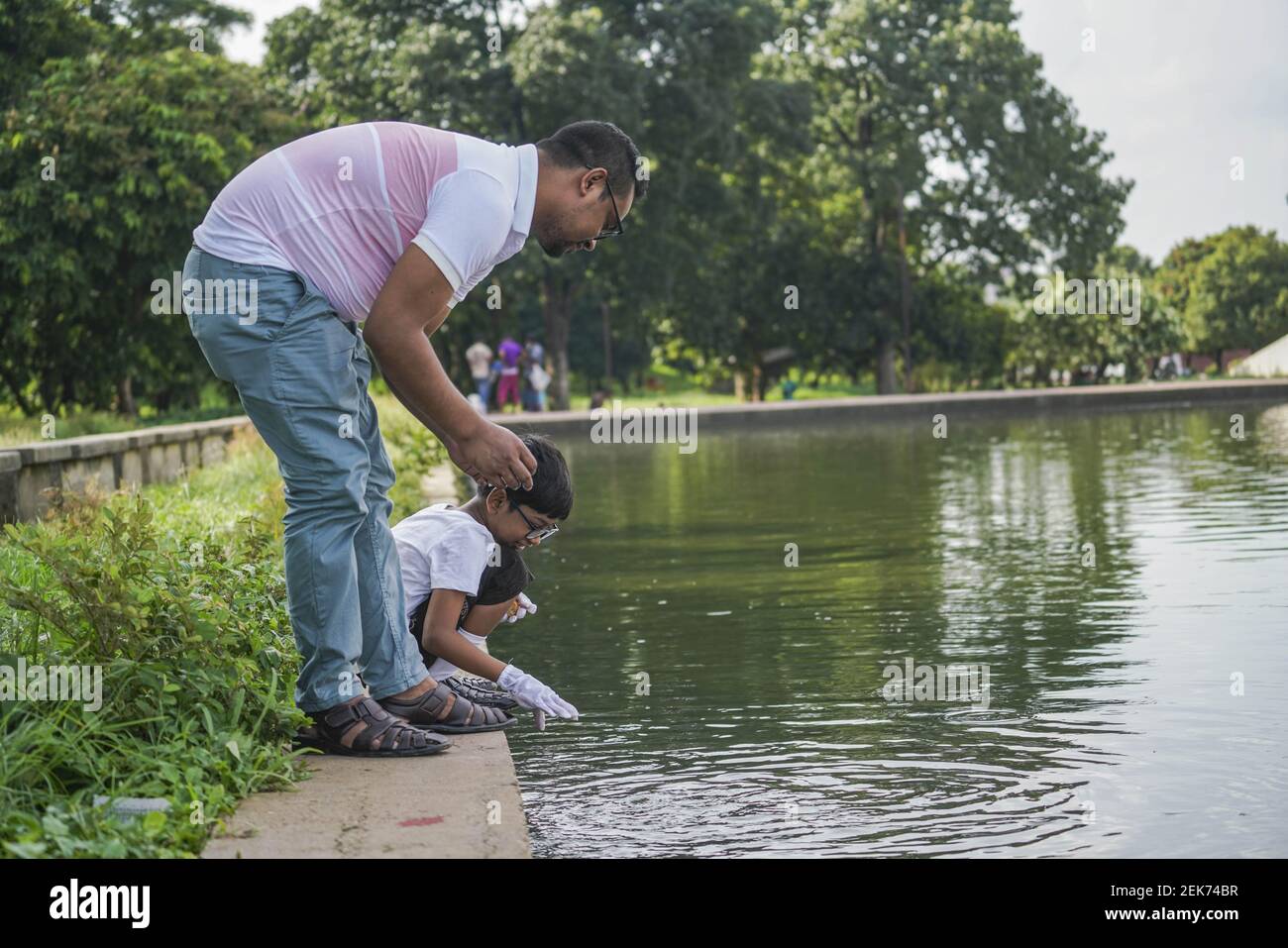 A father and son are seen feeding fish at Suhrawardy Udaan park during ...