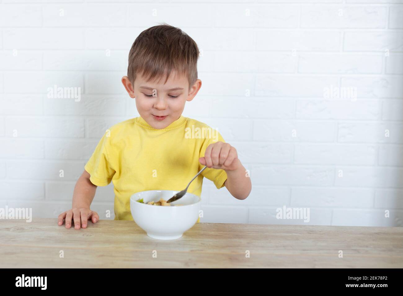 Little left-handed boy in a yellow T-shirt eating fruit salad and ...
