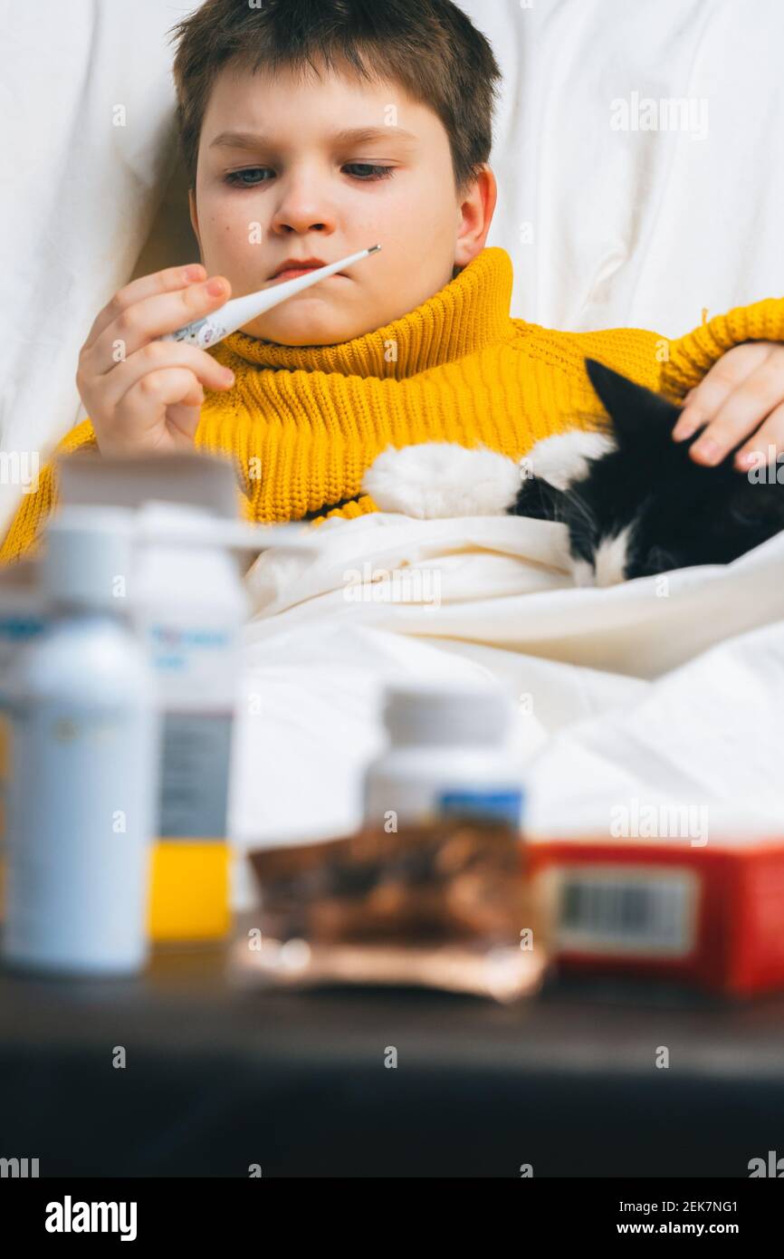 Sick child boy with digital thermometer in mouth lying in bed with ...