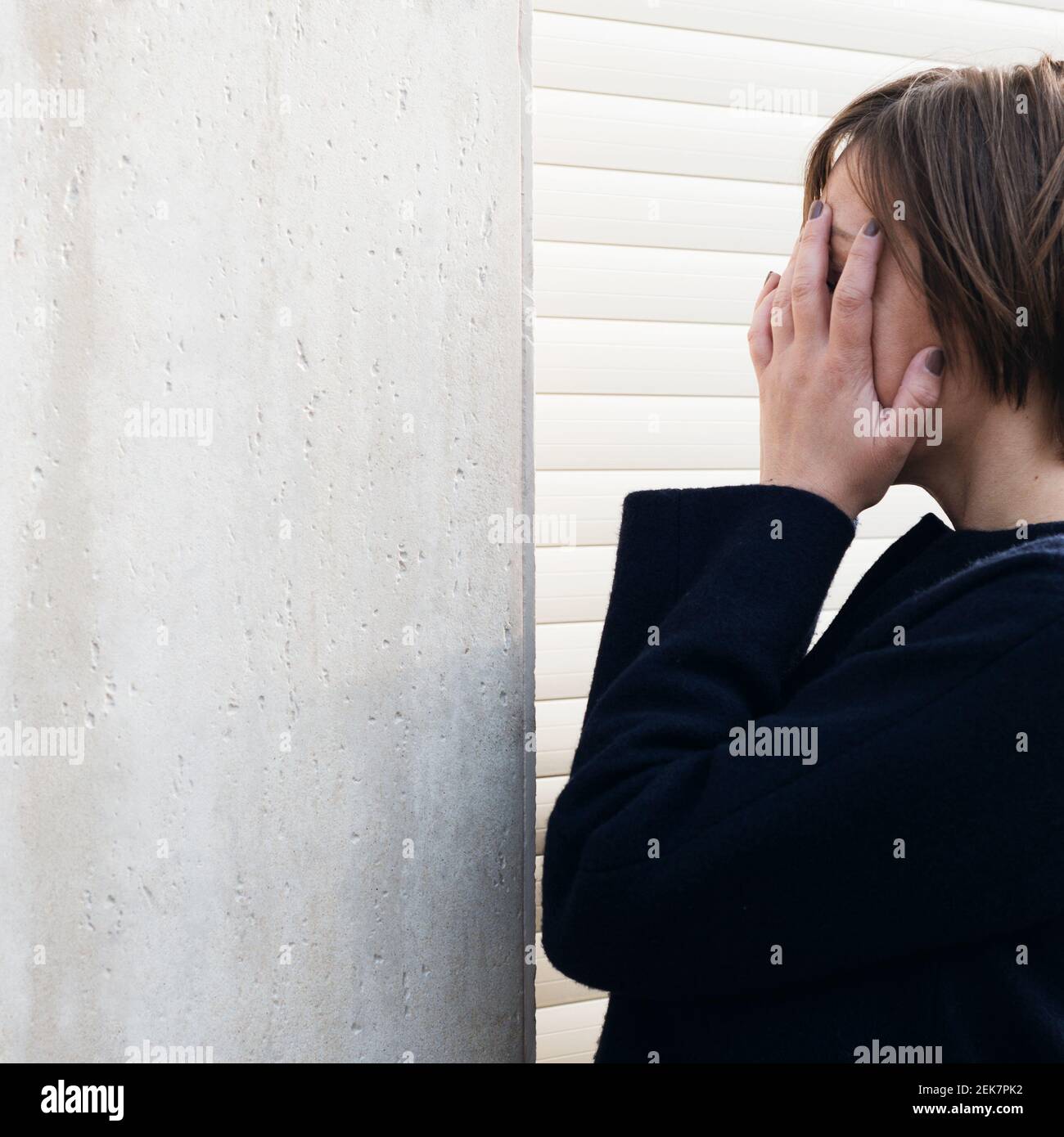 Woman is standing against a wall with her hands in her face Stock Photo ...