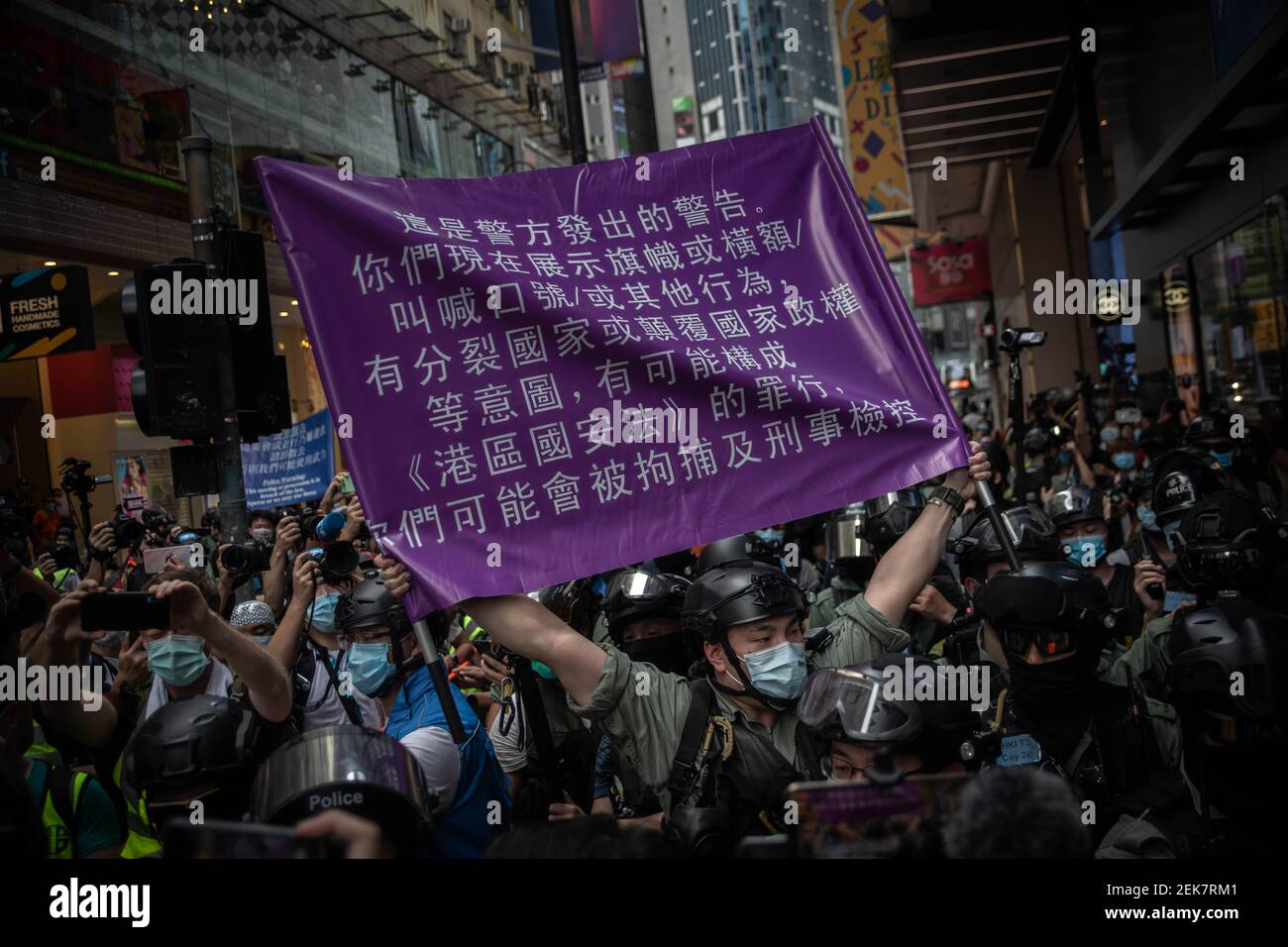 A group of riot police block the street and raise a warning flag during ...