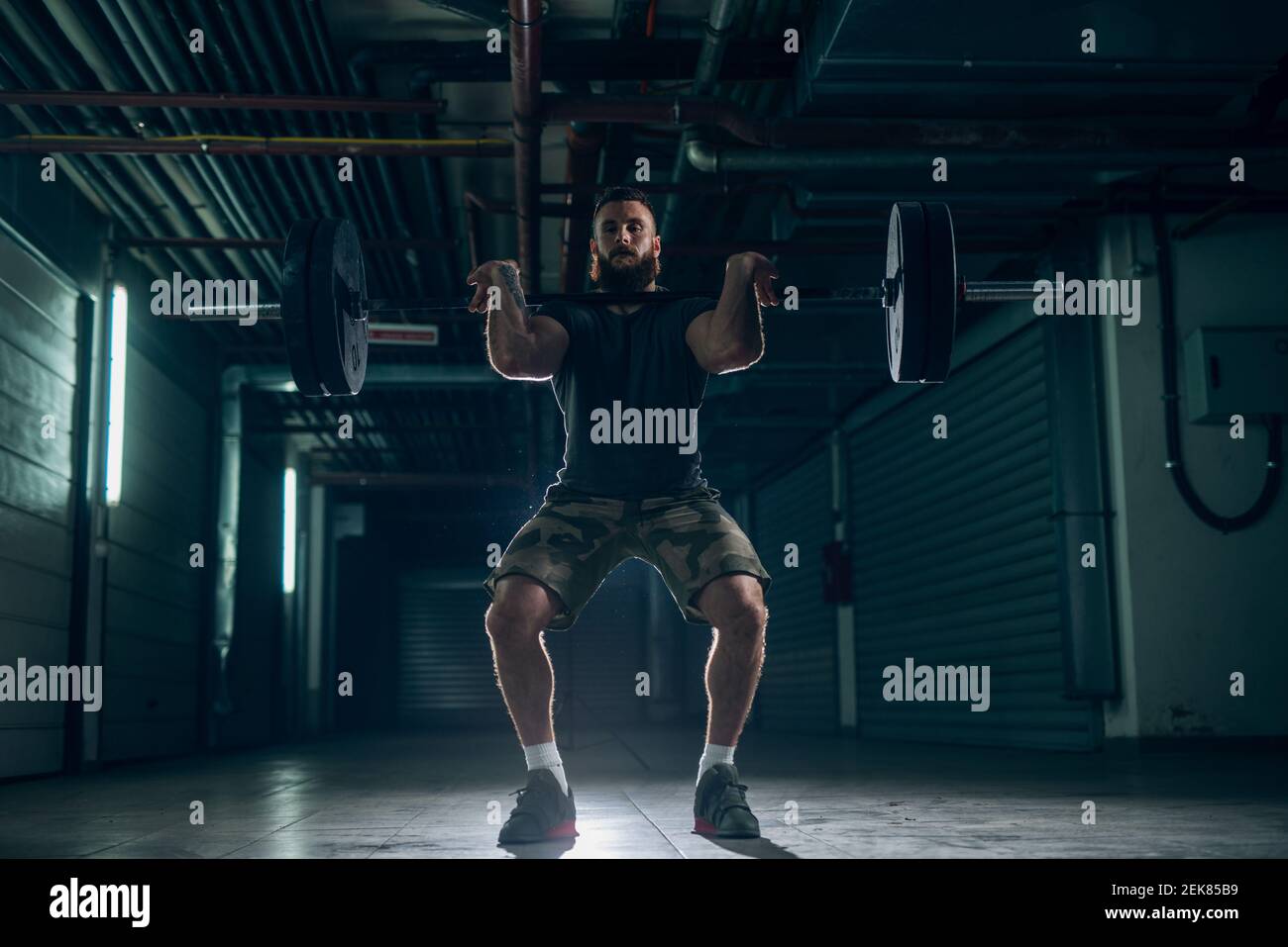 Strong bearded man doing workout, standing and lifting barbell indoors ...