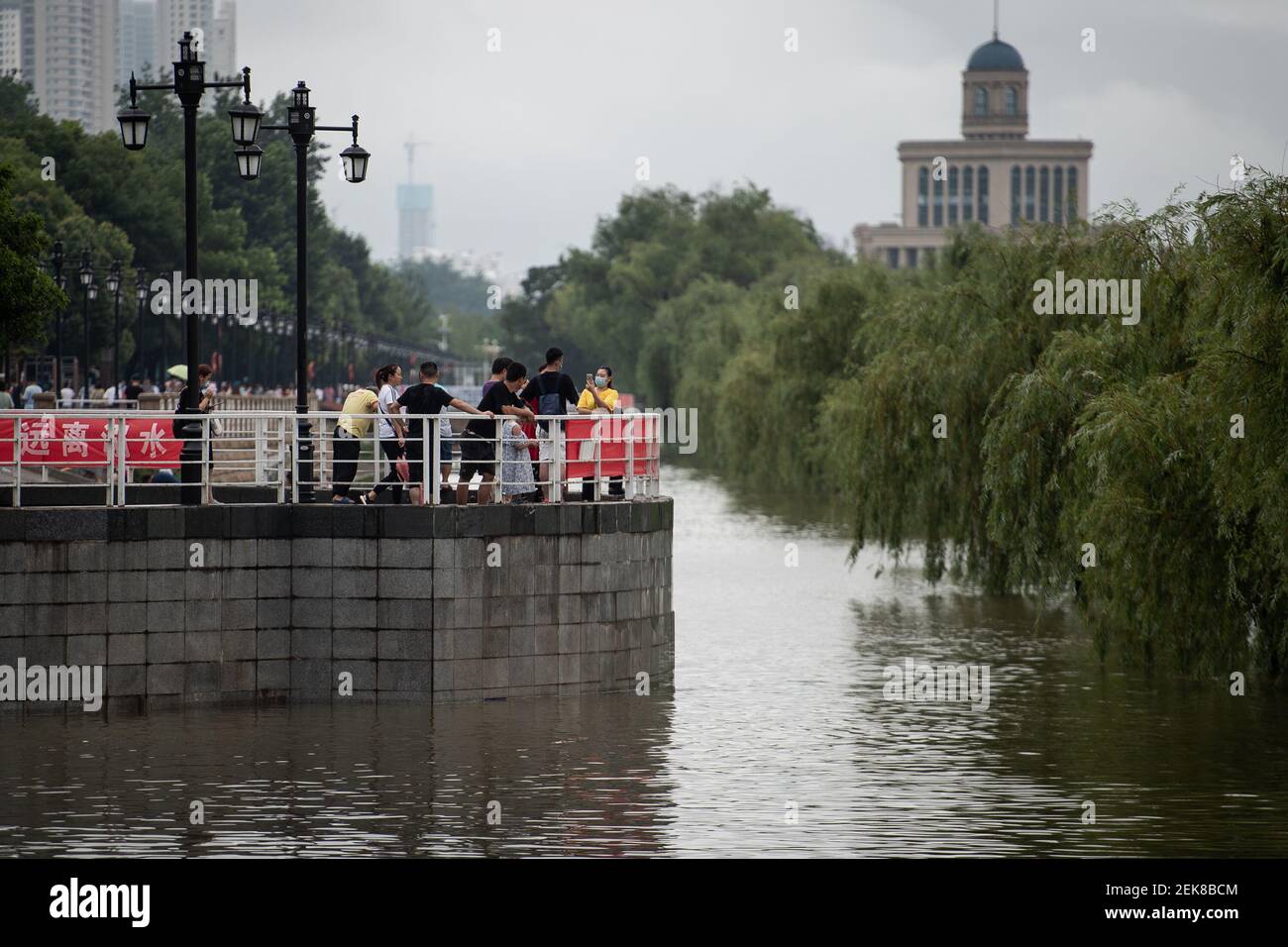 Citizens walk along the waterlogged riverside road in Wuhan city ...