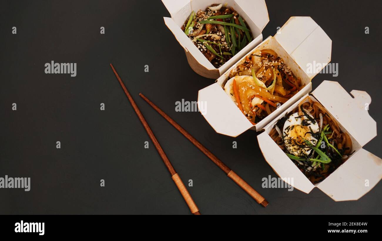 Noodles with pork and vegetables in take-out box on black table. Asian ...