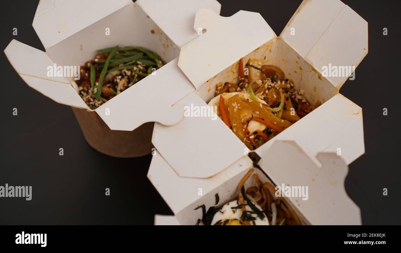 Noodles with pork and vegetables in take-out box on black table. Asian ...