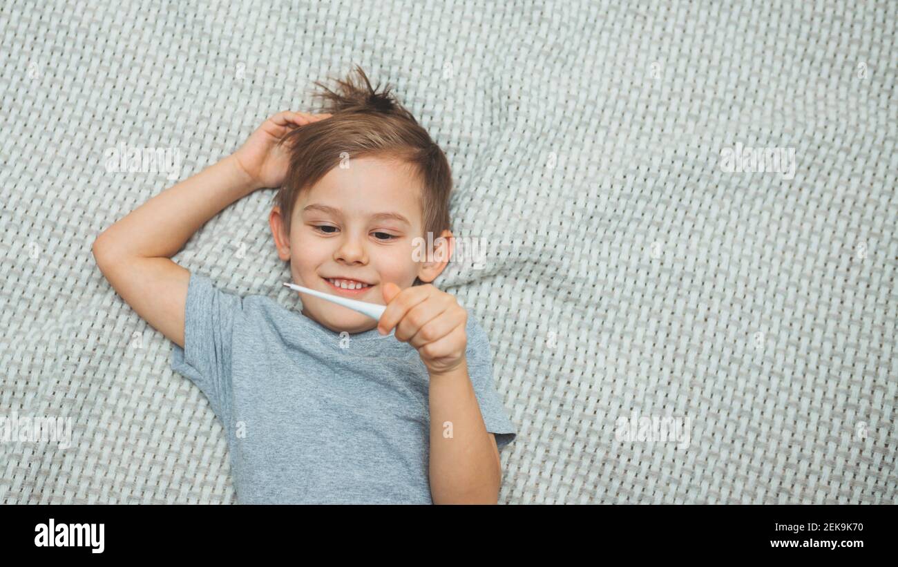 Little boy lying on the bed holding a thermometer in his hand and ...