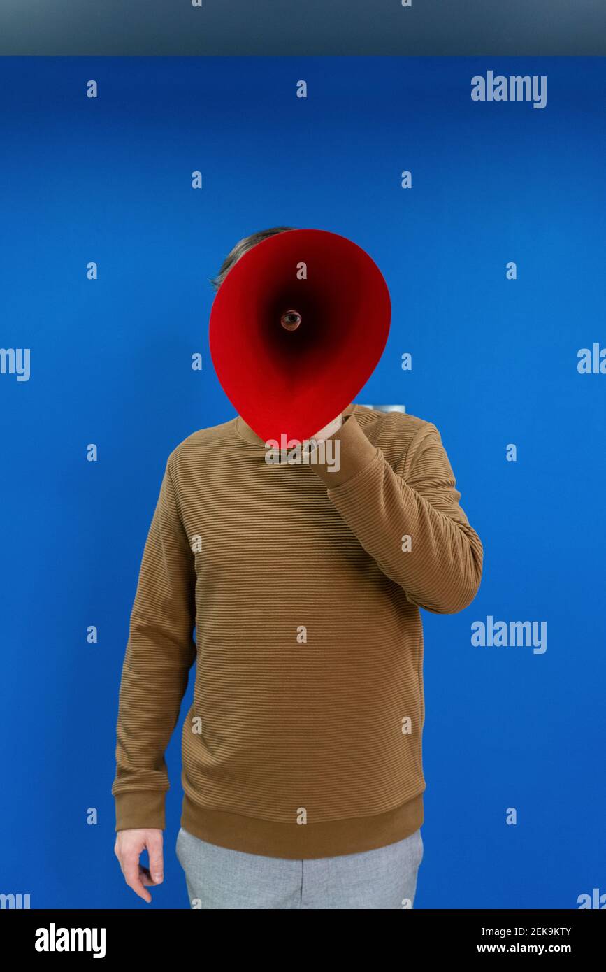 Mid adult businessman looking through megaphone against blue wall at ...