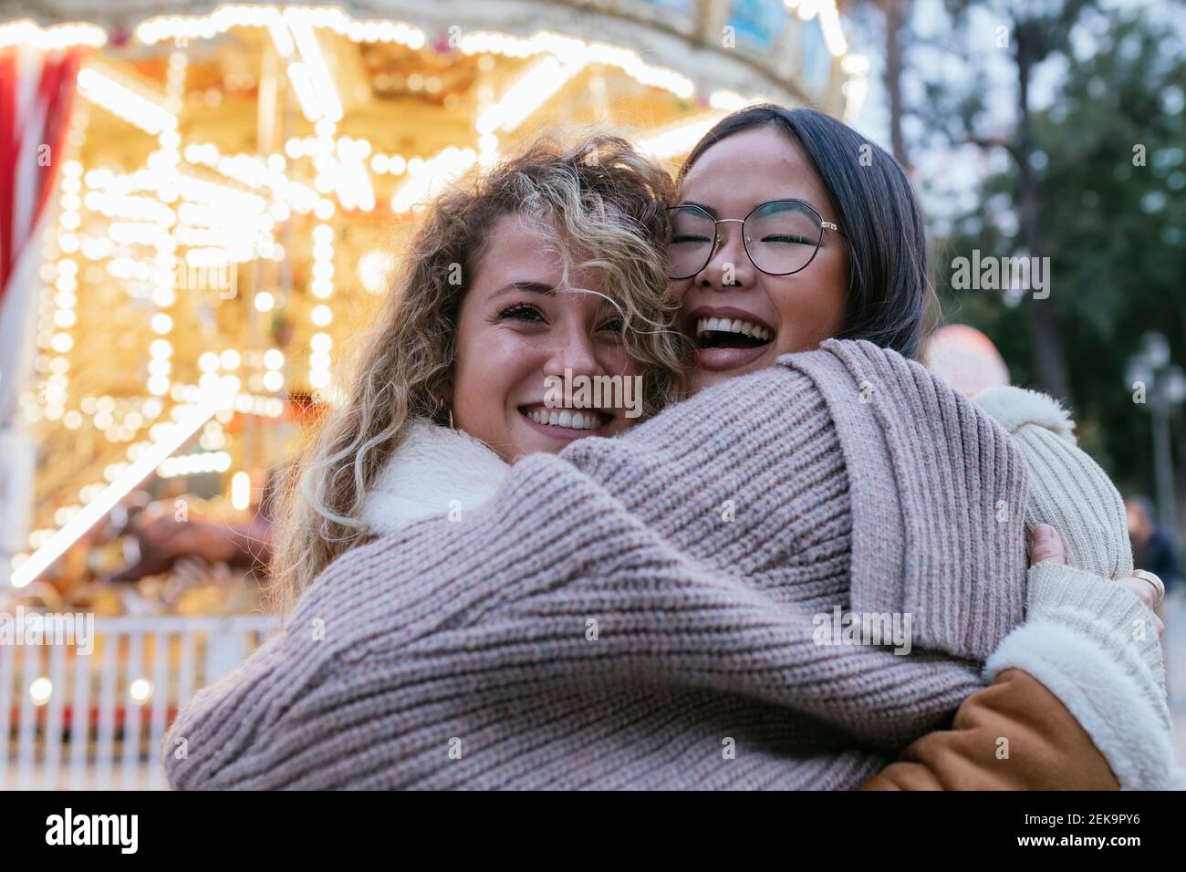 Laughing female friends embracing against illuminated carousel Stock ...