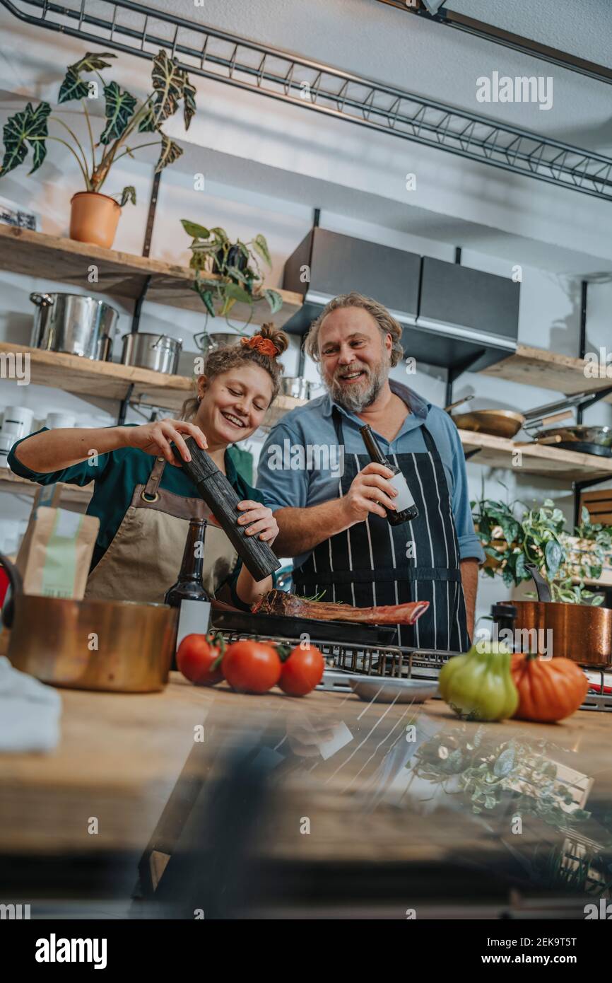 Female chef adding pepper on food while standing by colleague drinking ...