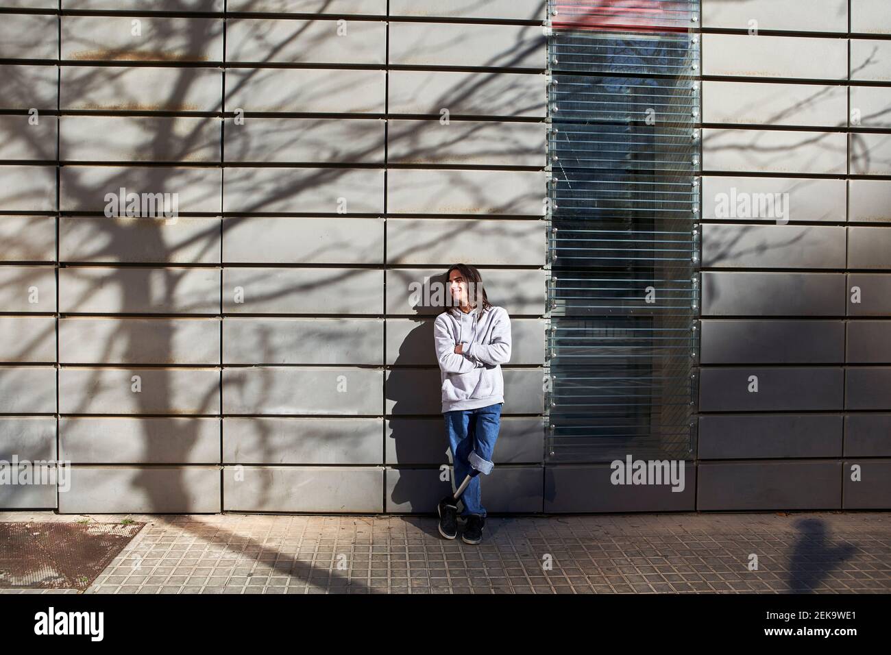 Disabled man with arms crossed standing against wall with tree shadow ...