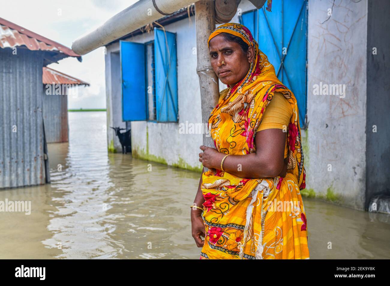 A woman poses in front of her flooded house. At least 1.5 million ...