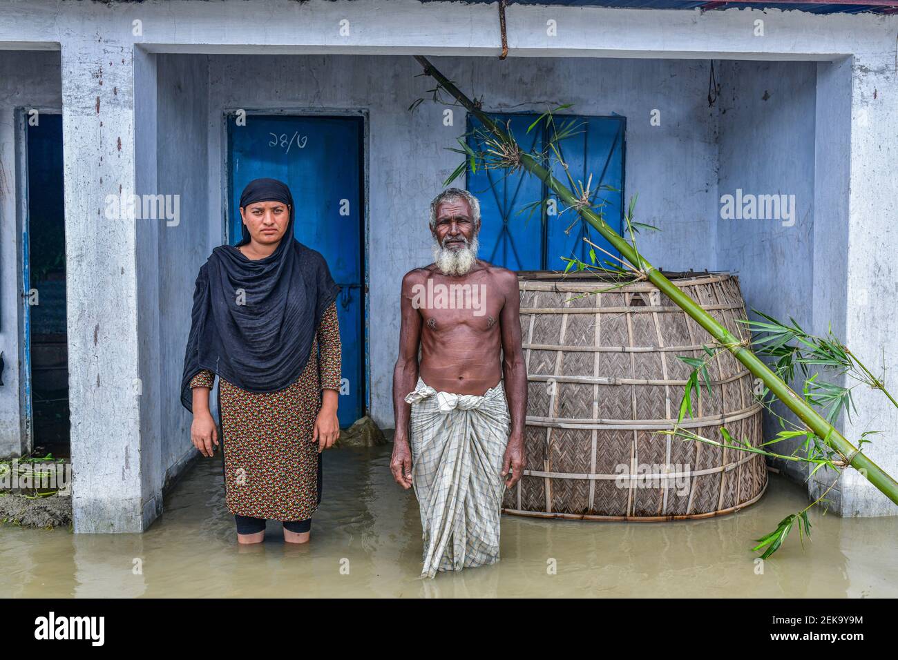 A man with his daughter pose in front of their flooded house. At least ...