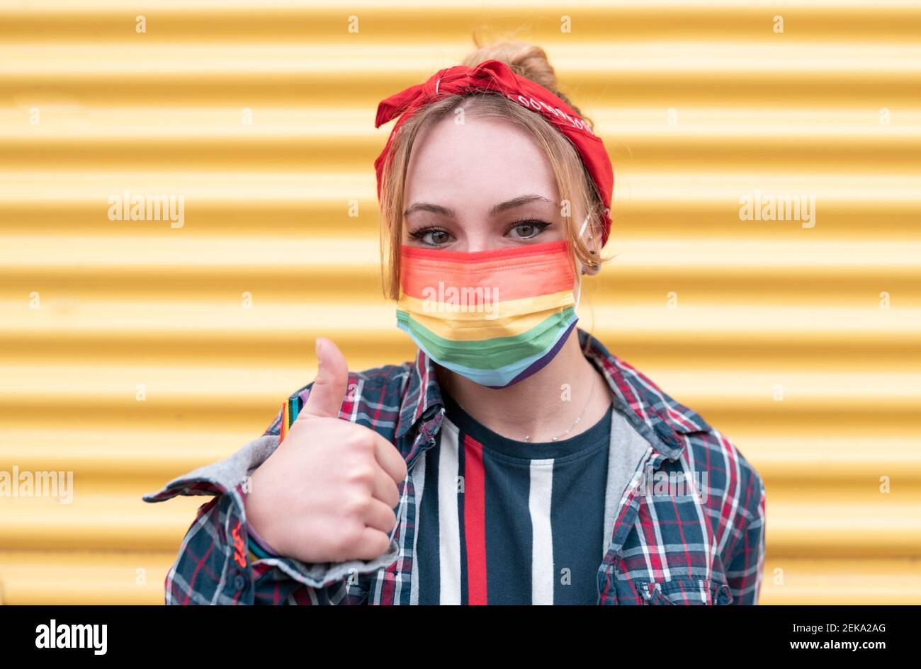 Young woman wearing multi colored face mask gesturing thumbs up while ...
