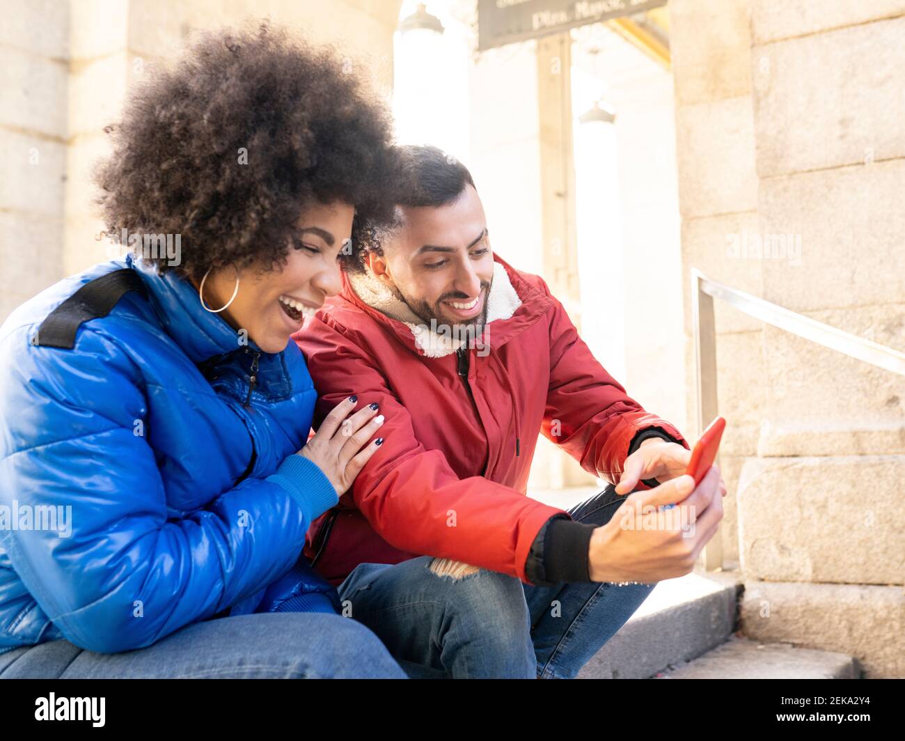 Happy friends using smart phone while sitting on steps Stock Photo - Alamy