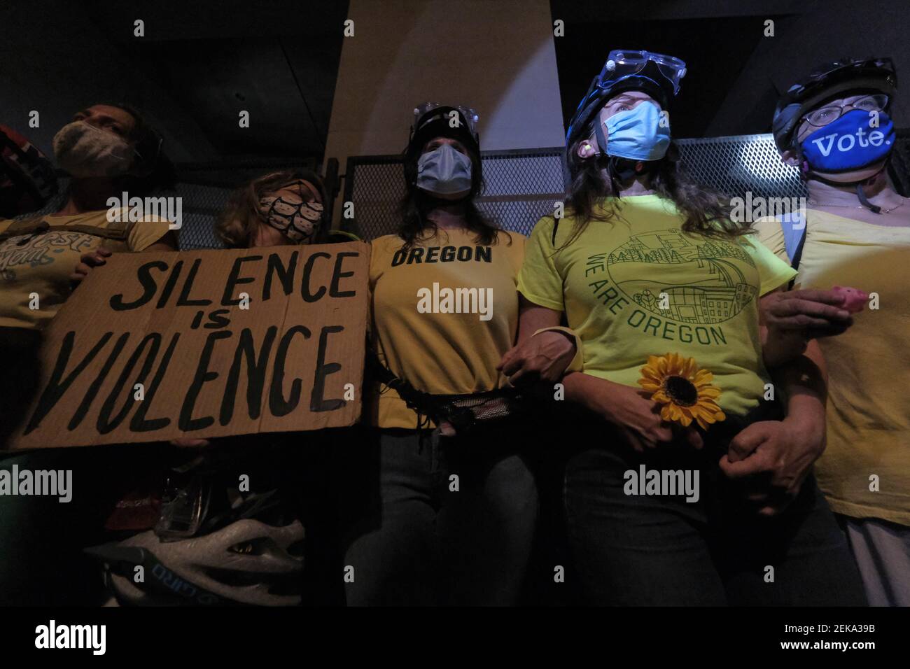 Moms with interlocking arms stand with their backs up against a fence ...