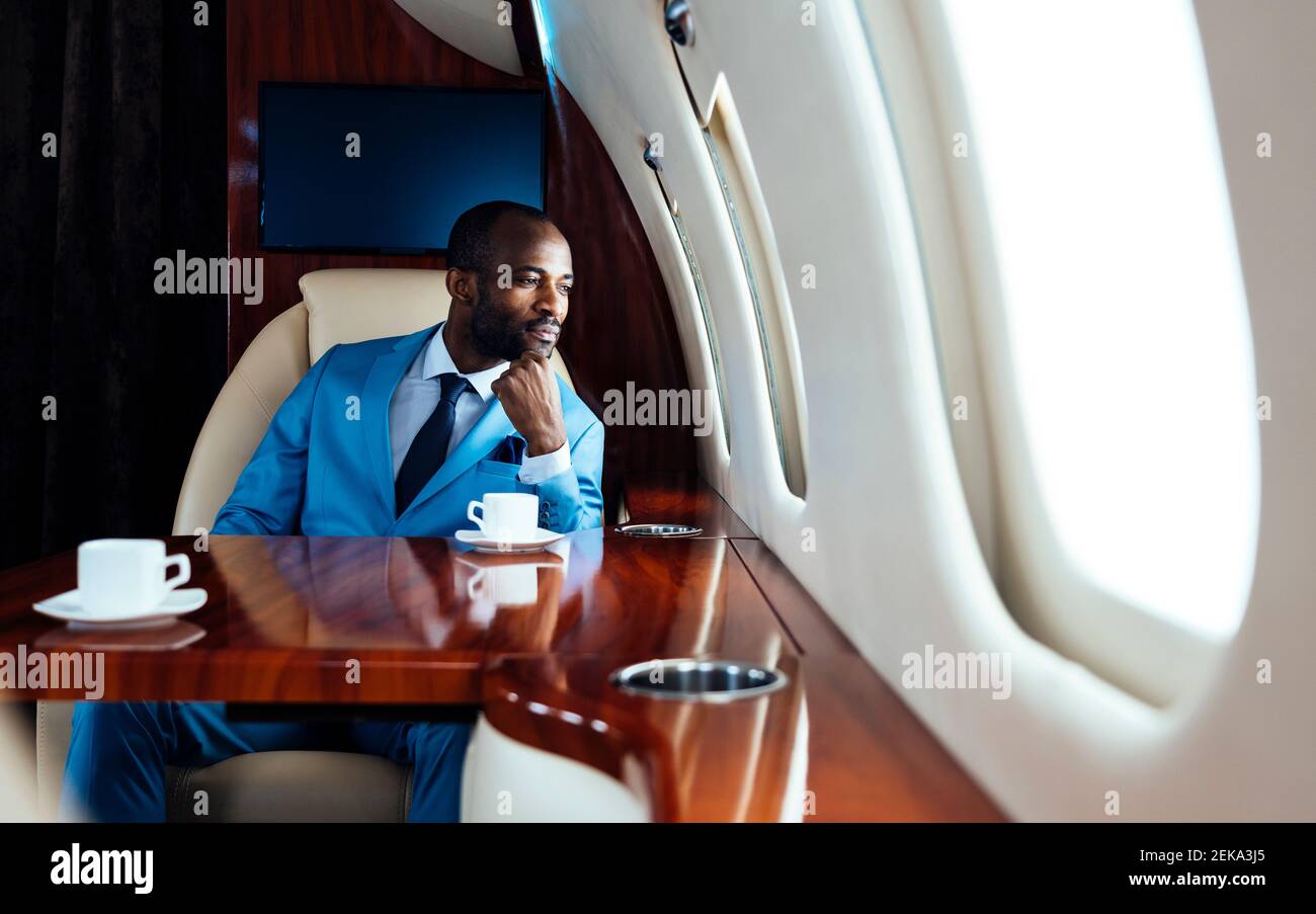 Young businessman with hand on chin looking through window while ...