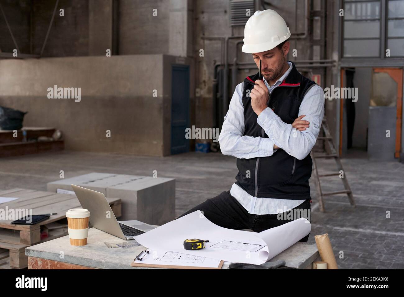 Male architect thinking while analyzing blueprint on table in building ...