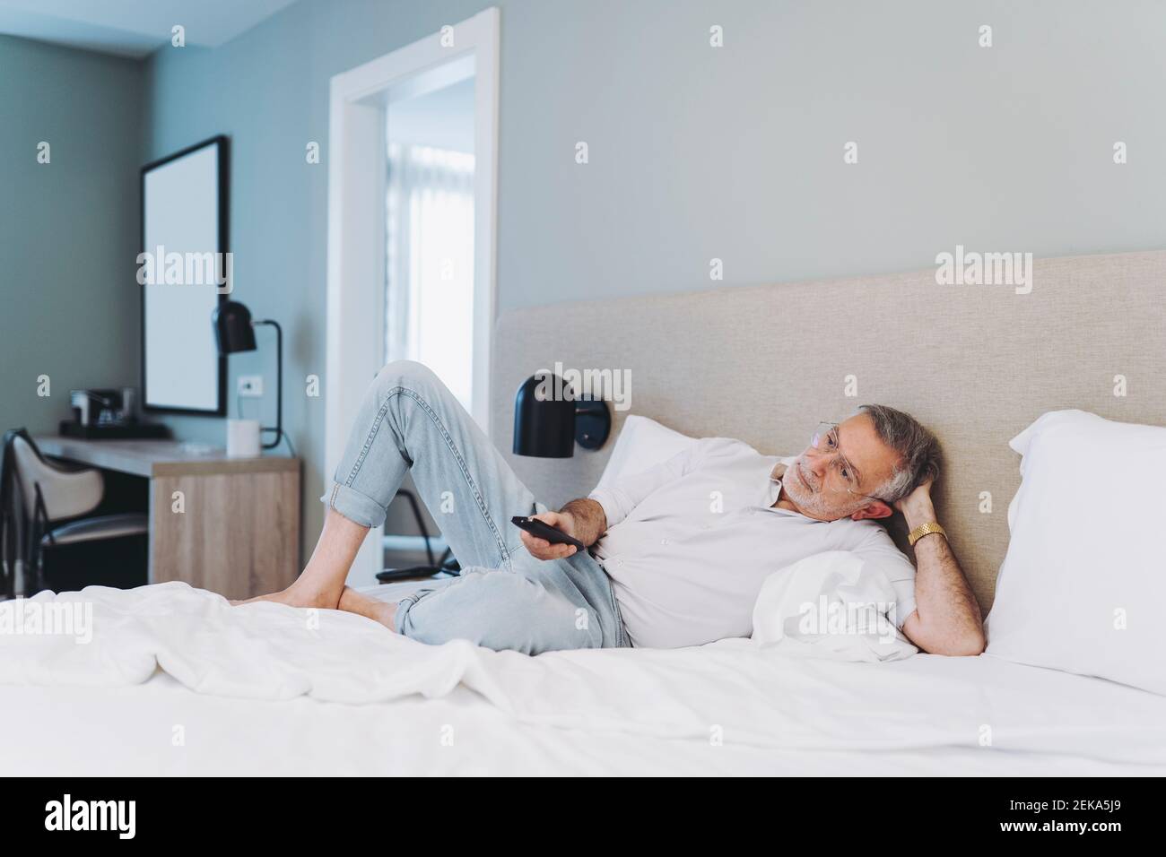 Relaxed man using remote control while lying on bed in hotel room Stock ...