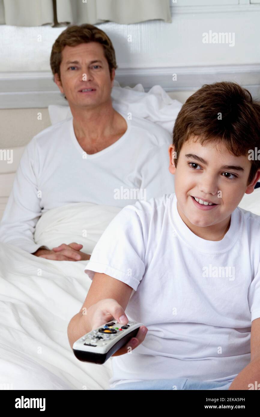 Boy changing channels with a remote control with his father in the ...
