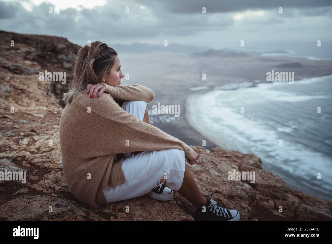 Young woman looking at Famara Beach while sitting on mountain at ...