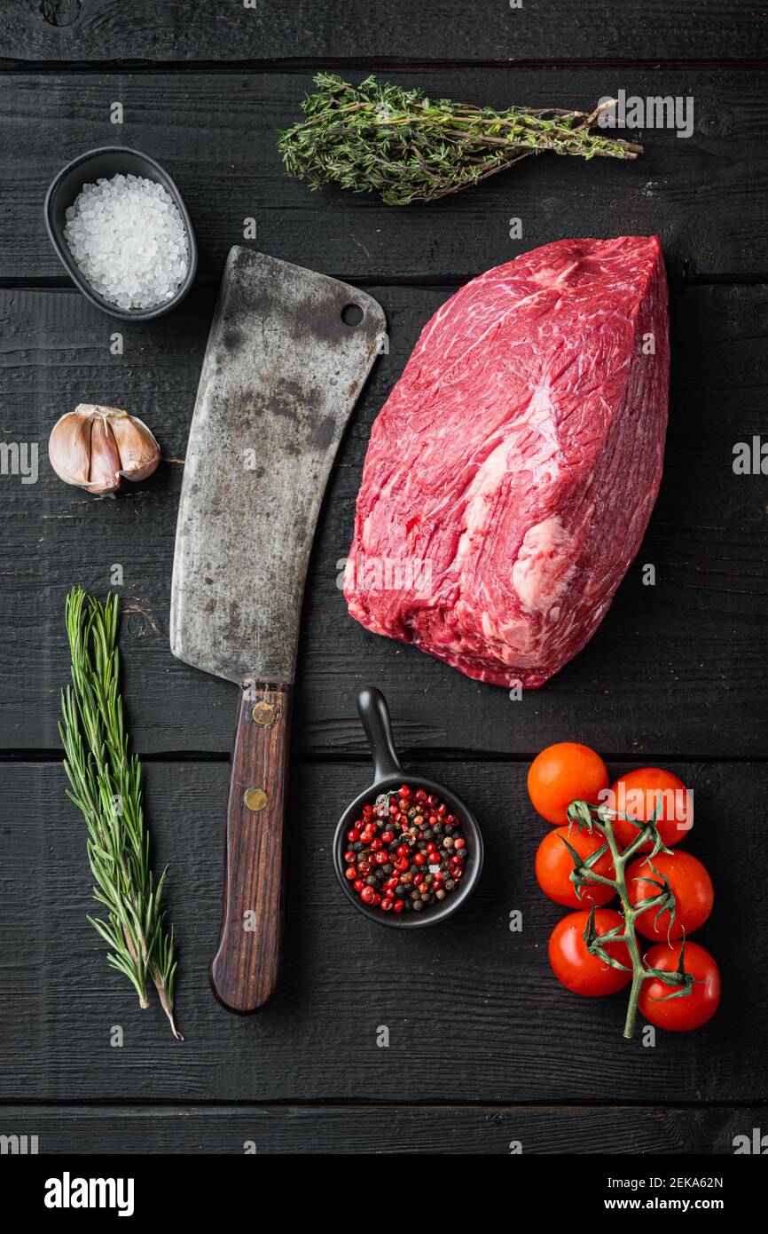 Round beef meat raw set with old butcher cleaver knife, on black wooden ...