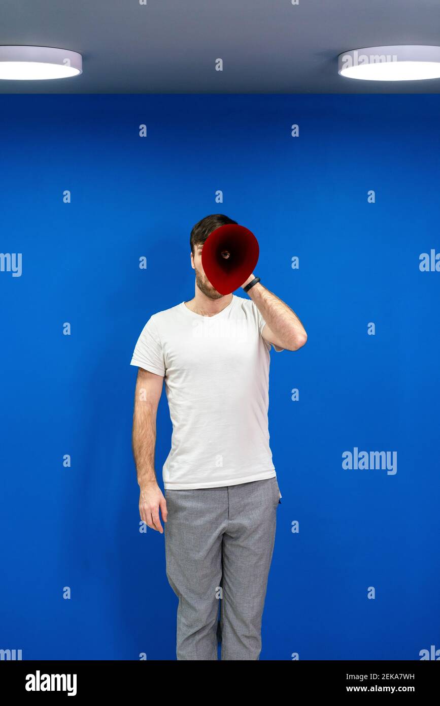 Creative businessman looking through megaphone while standing against ...