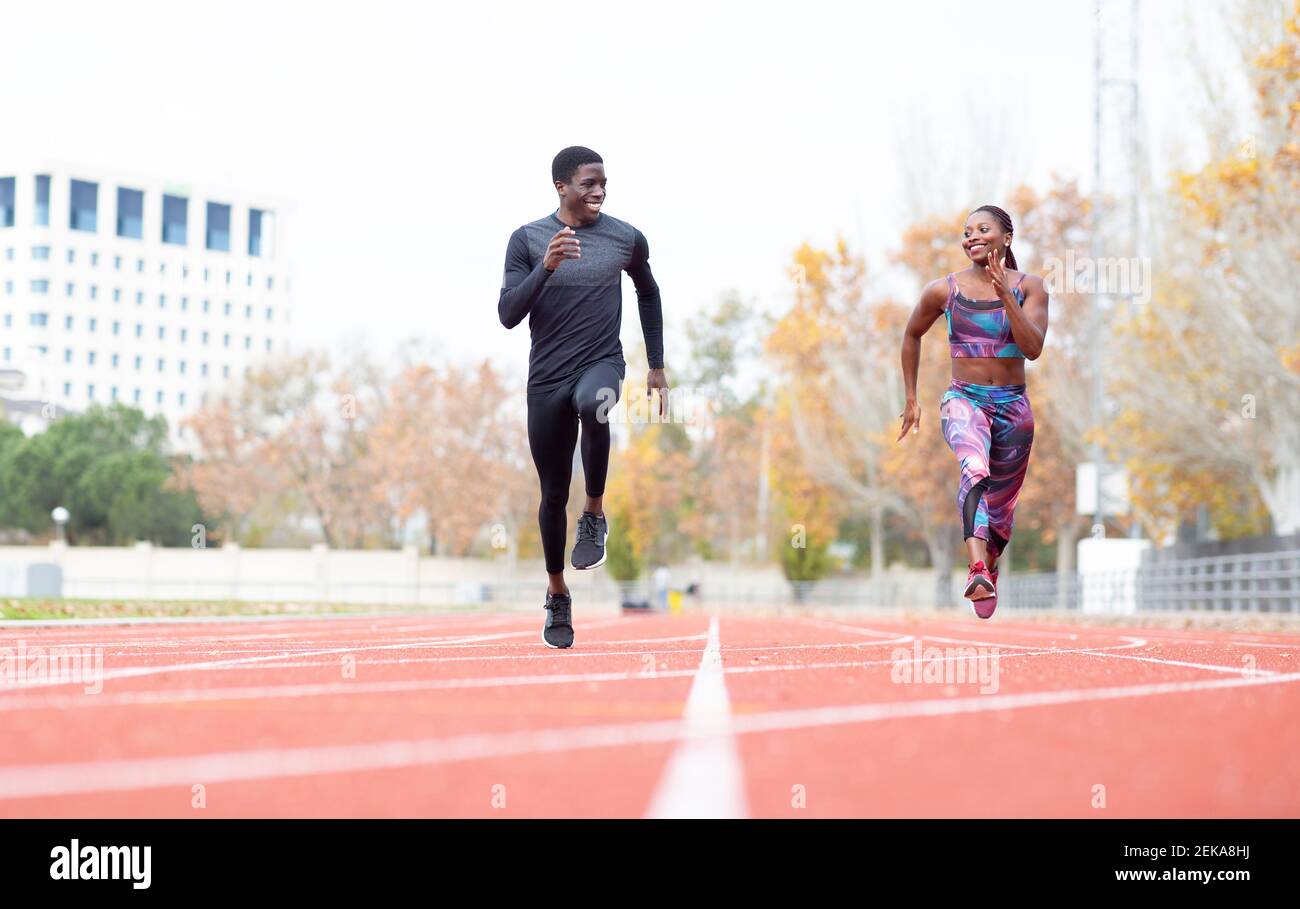Happy male and female athlete running on track against clear sky Stock ...