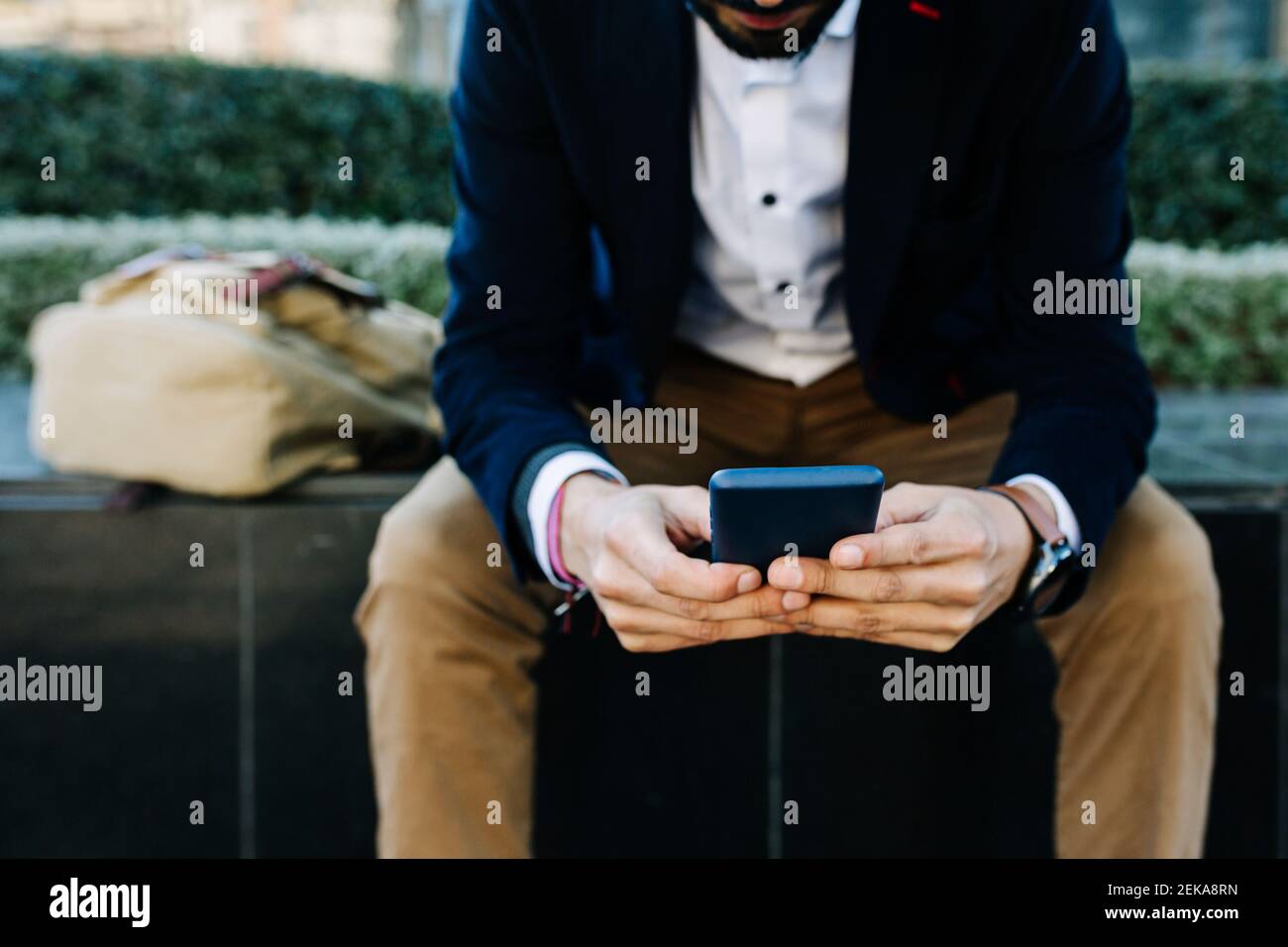 Businessman using smart phone while sitting on bench Stock Photo - Alamy