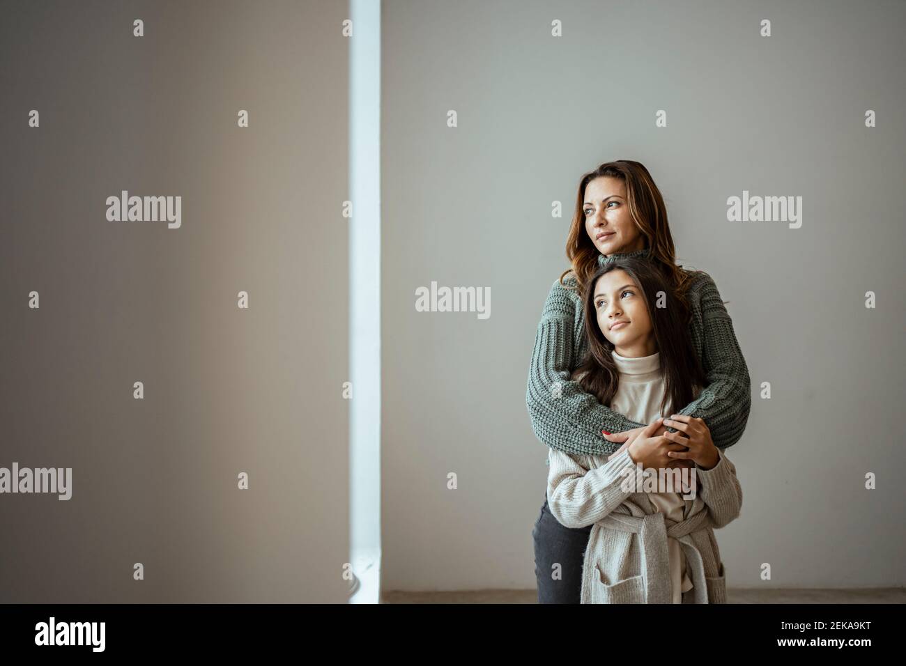 Mother and daughter looking away while embracing each other against ...