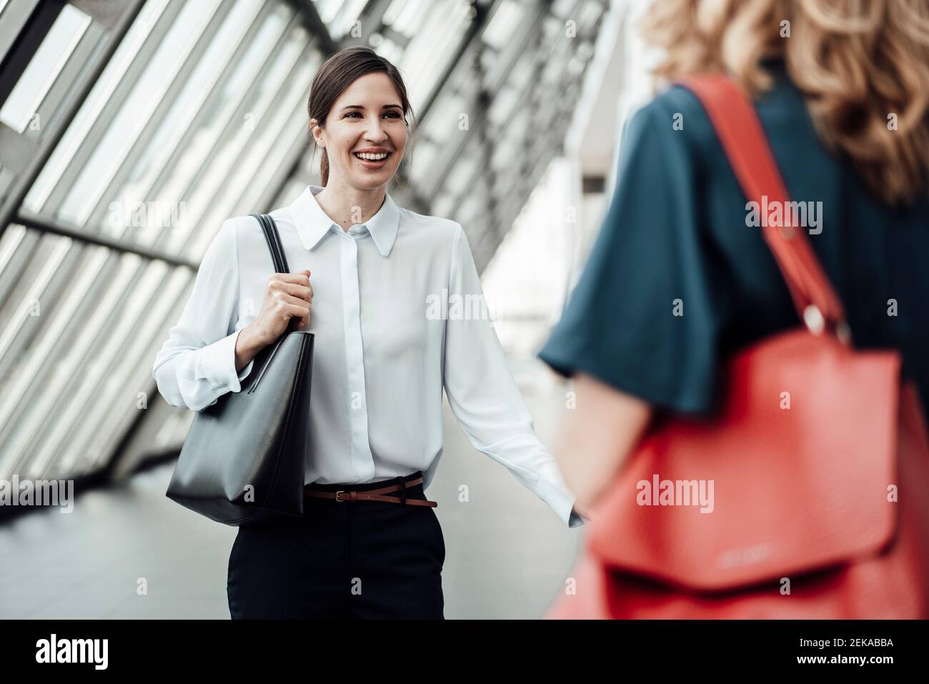 Smiling businesswoman talking with female colleagues in office corridor ...