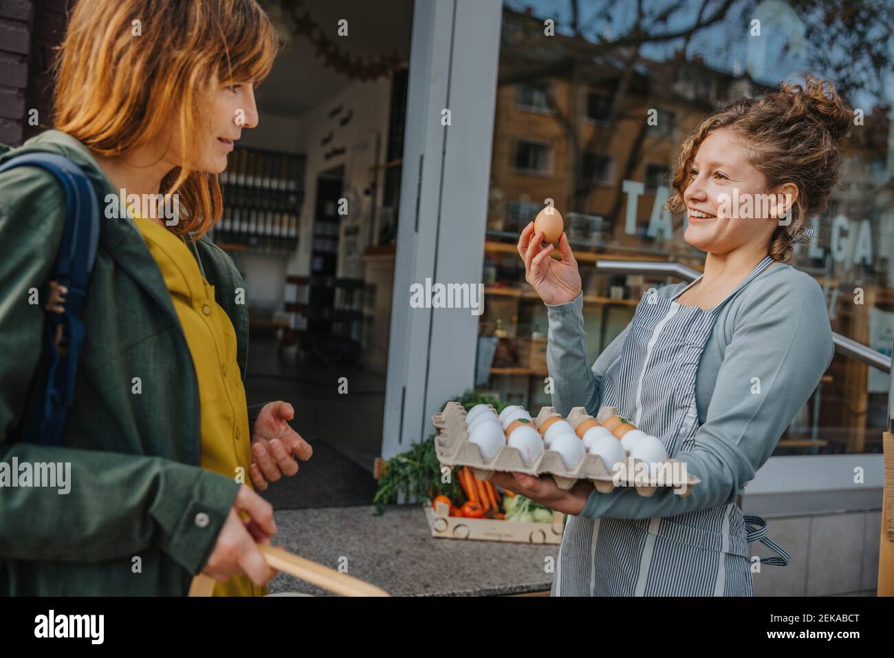 Store owner selling eggs to mature female customer at organic food shop ...