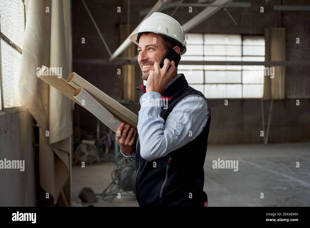 Smiling male building contractor talking over smart phone inside ...