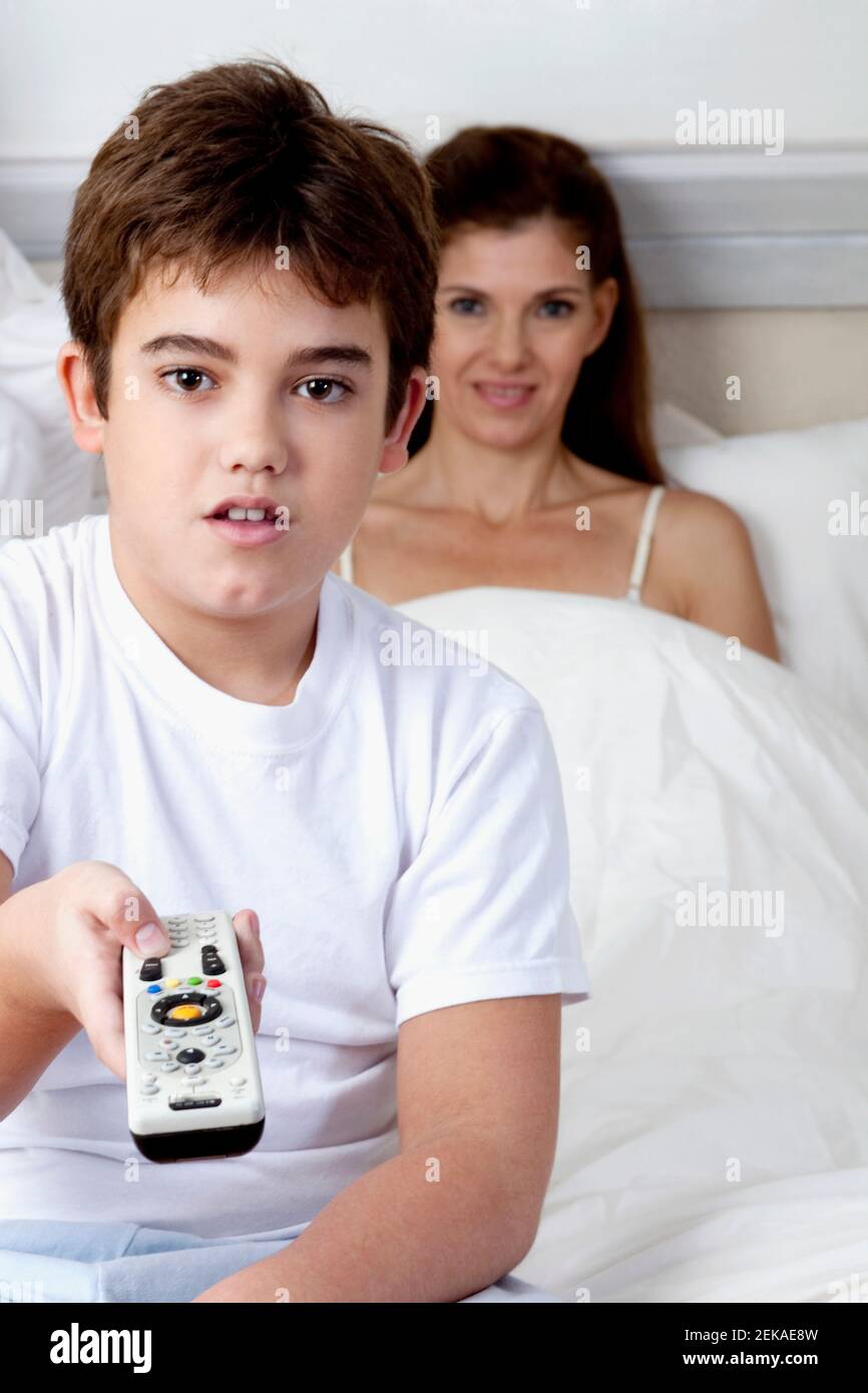 Boy changing channels with a remote control with his mother in the ...