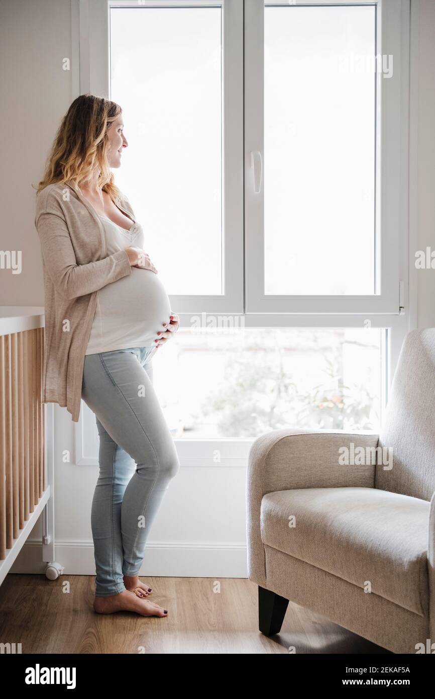 Pregnant woman with hands on stomach standing by window Stock Photo - Alamy