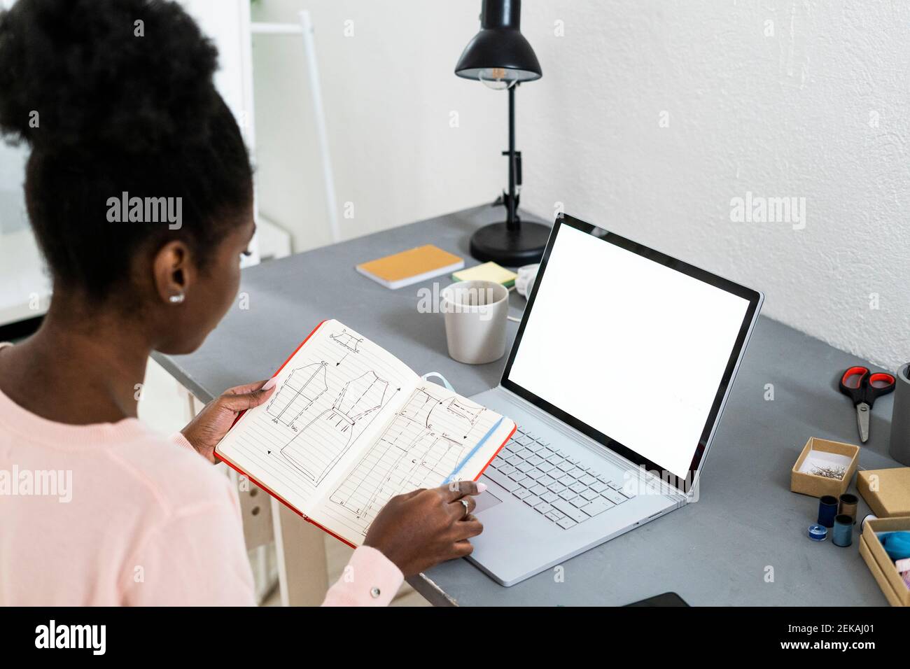Fashion stylist with laptop analyzing diagram in book while sitting at ...