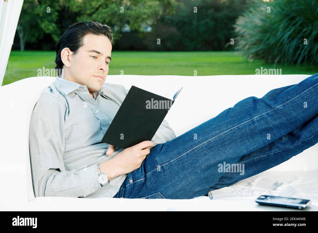 Man leaning on a couch and reading a book Stock Photo - Alamy